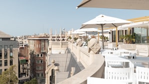 Terraço no telhado com área de estar externa, vista panorâmica da cidade e céu claro.