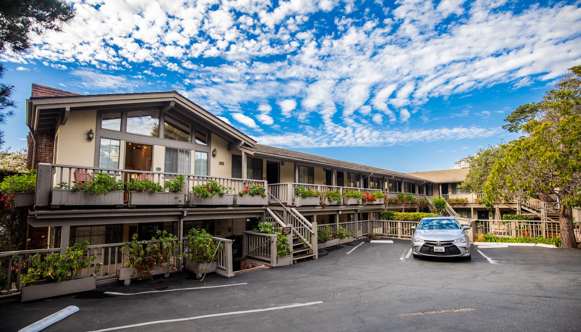 Um motel de vários andares com varandas, área de estacionamento e um carro estacionado na frente.