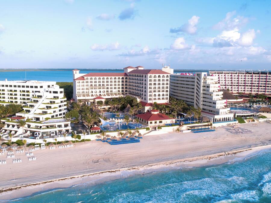 Um hotel à beira-mar com vários edifícios, piscina e guarda-sóis de praia.