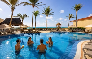 Piscina com espreguiçadeiras e palmeiras, sob um céu claro e com vista para o oceano.
