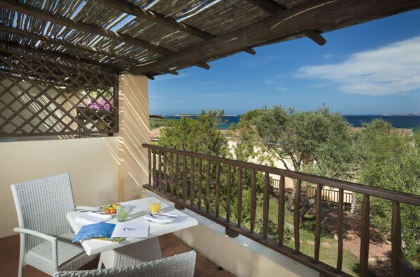 Varanda com uma mesa posta para dois, com vista panorâmica para o mar e vegetação.