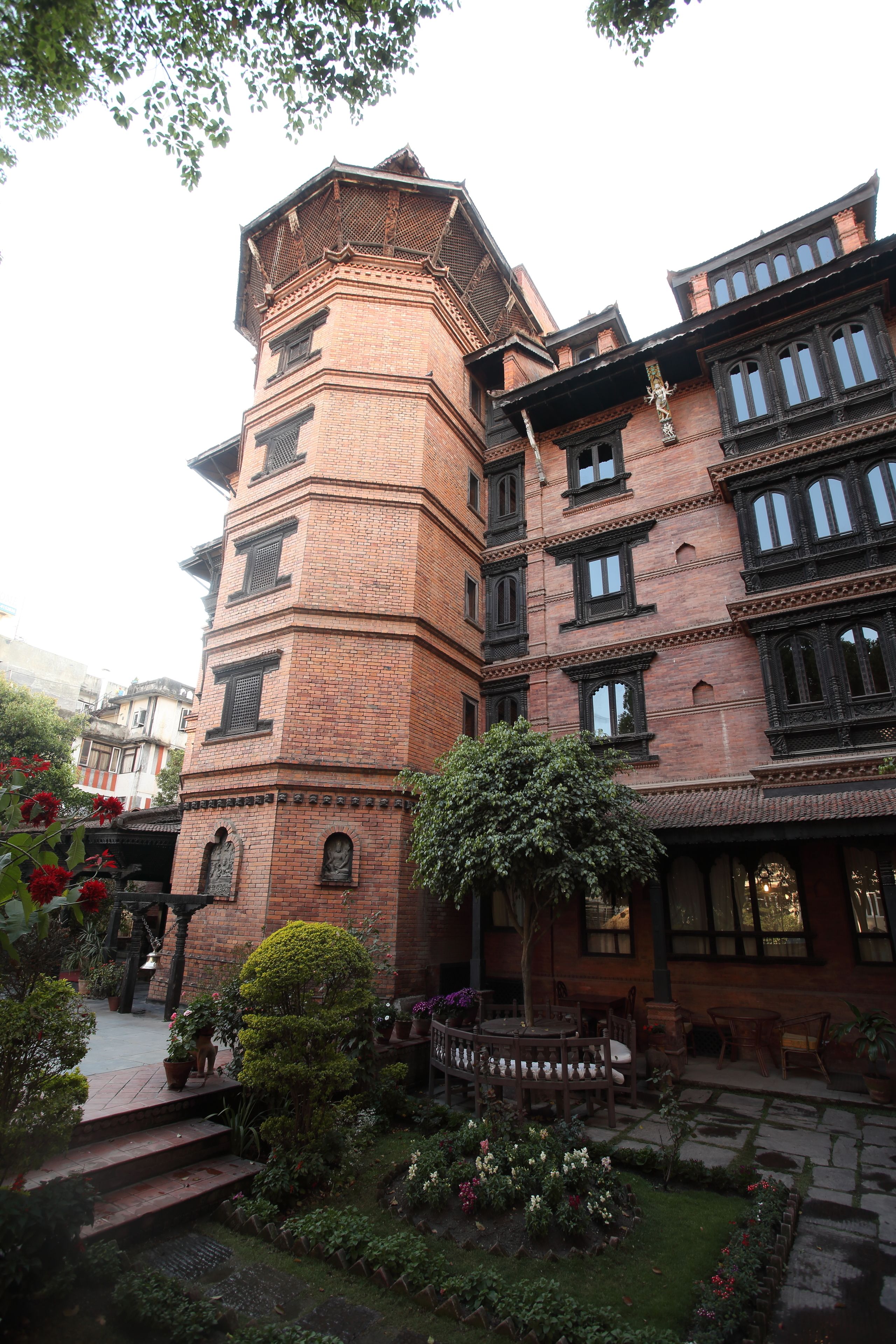 Um edifício tradicional com uma torre, várias janelas e um jardim com plantas em vasos e um banco.