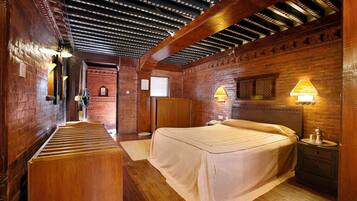 Quarto com piso de madeira, cama com cabeceira, mesa de cabeceira, abajur e parede de tijolos.