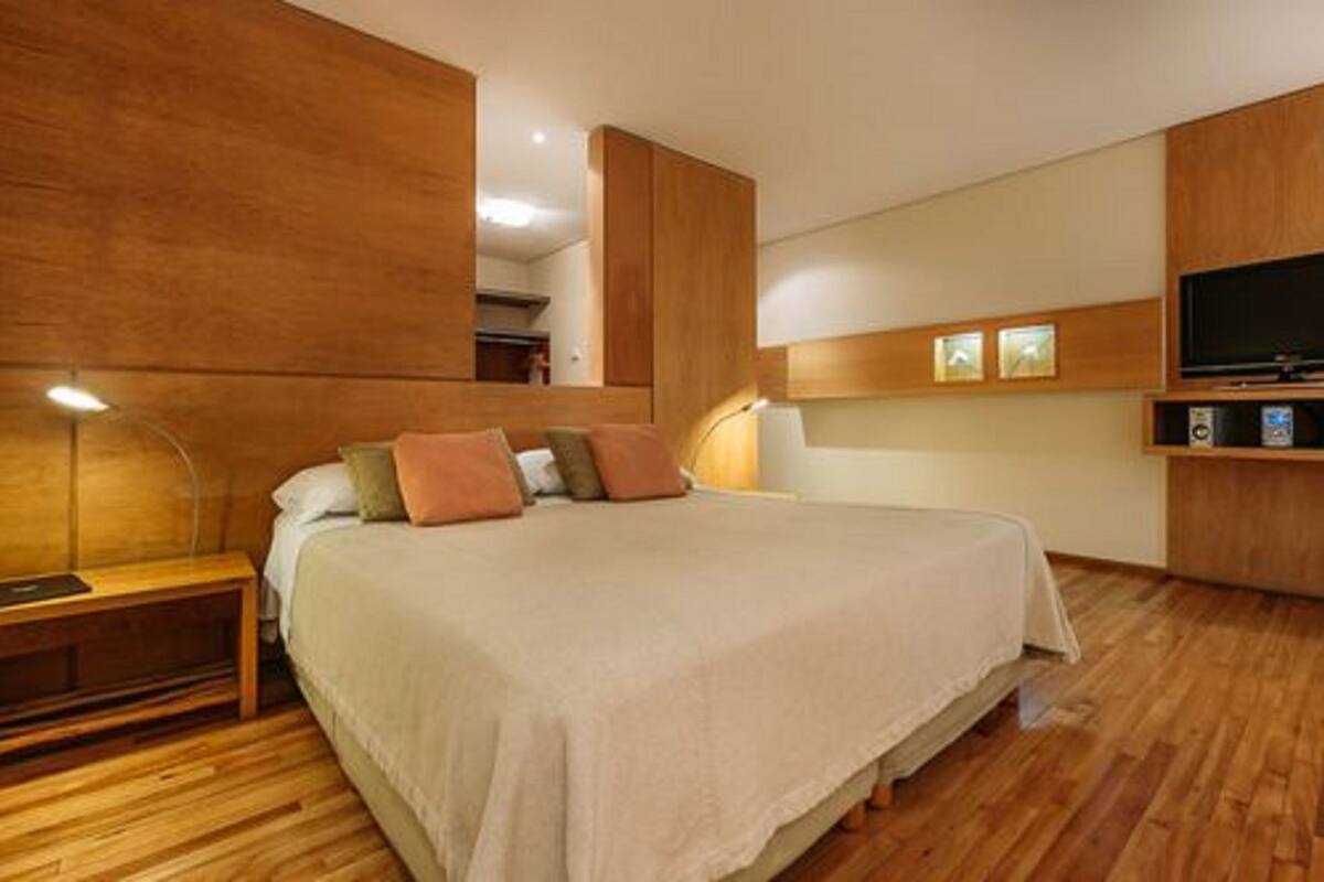 Quarto moderno com uma cama grande, cabeceira de madeira, mesas de cabeceira, uma televisão e piso de madeira.