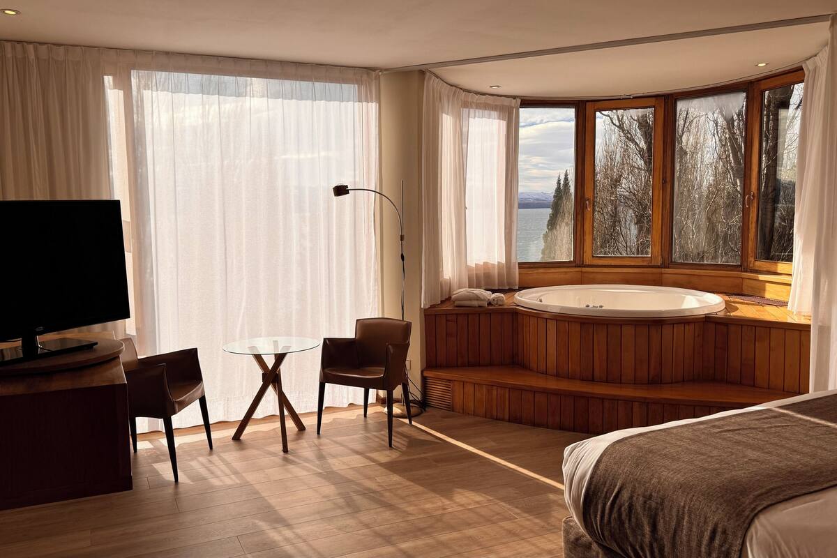 Quarto de hotel com televisão grande, uma mesa pequena com cadeiras, banheira e uma cama.