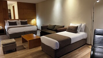 Quarto de hotel com uma cama, dois sofás, uma mesa de centro e uma cadeira.