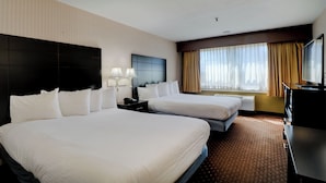 Quarto de hotel com duas camas, televisão, escrivaninha e janela com cortinas.