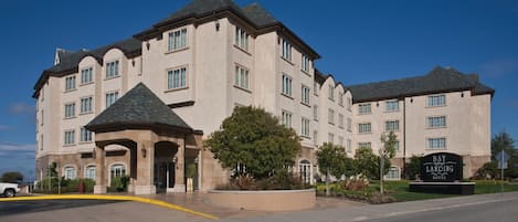 Um hotel grande, com vários andares, uma entrada imponente e uma alameda arborizada.