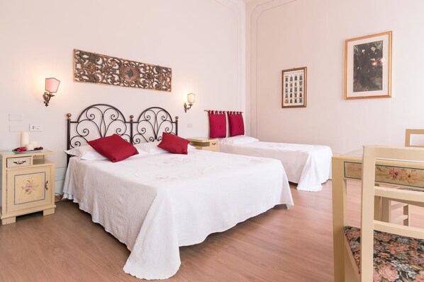 Quarto de hotel com duas camas, piso de madeira, uma secretária pequena e uma cadeira.