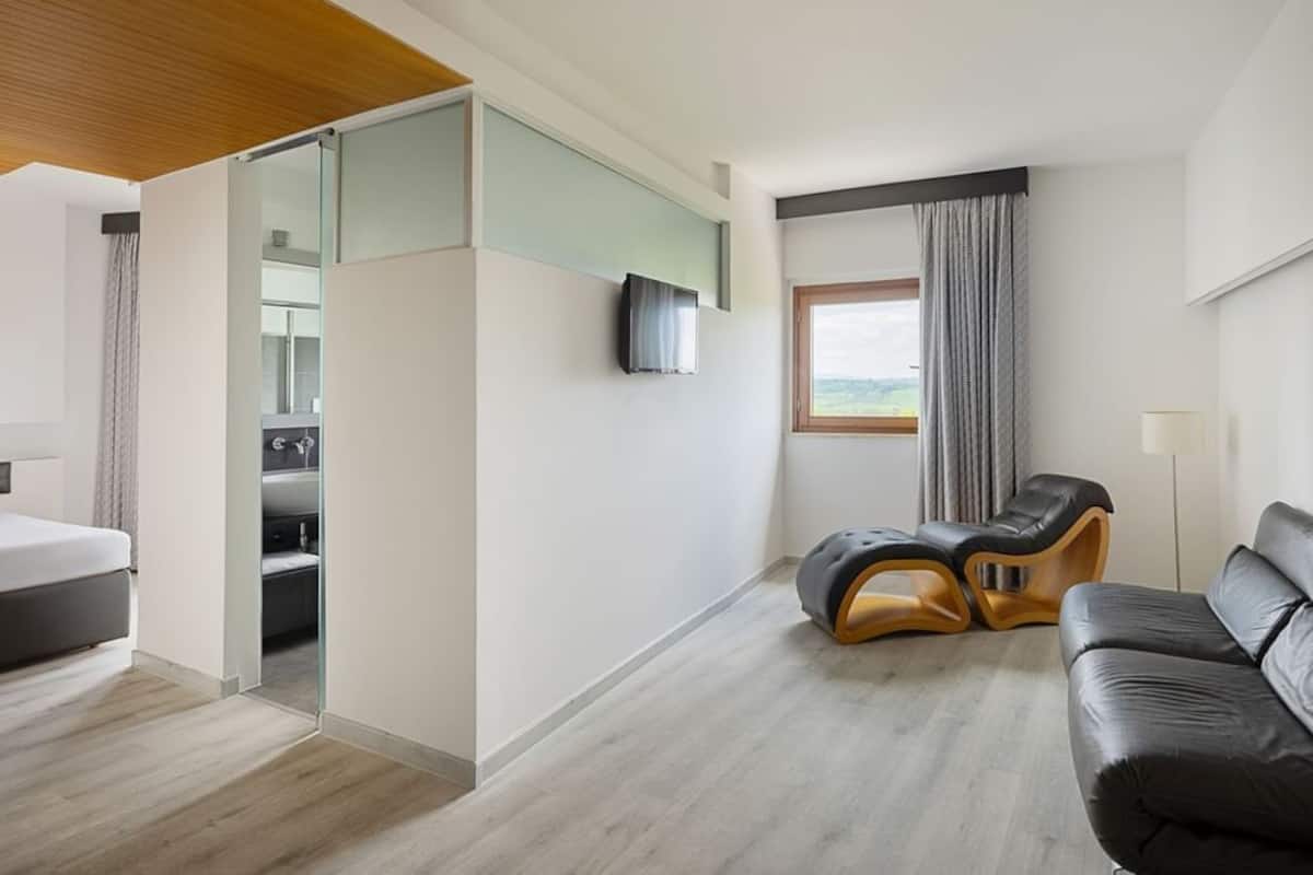 Quarto de hotel moderno com cama, sofá, TV e vista para o mar.
