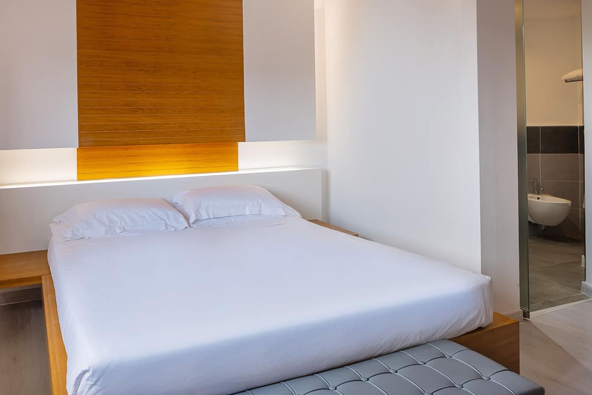 Quarto moderno com uma cama grande, painel de parede de madeira e porta de vidro para o chuveiro.
