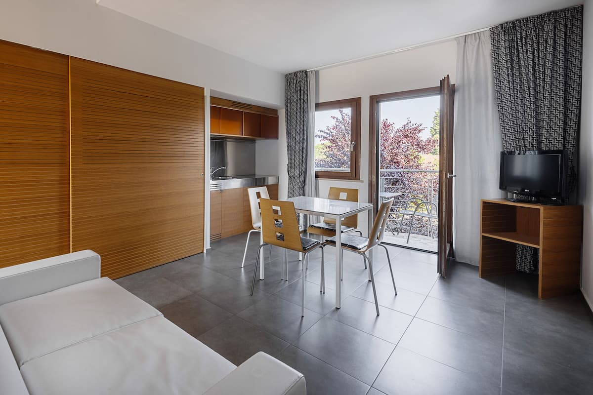 Uma sala de estar moderna com sofá, mesa de jantar, cadeiras, rack para TV e cozinha com armários e fogão.