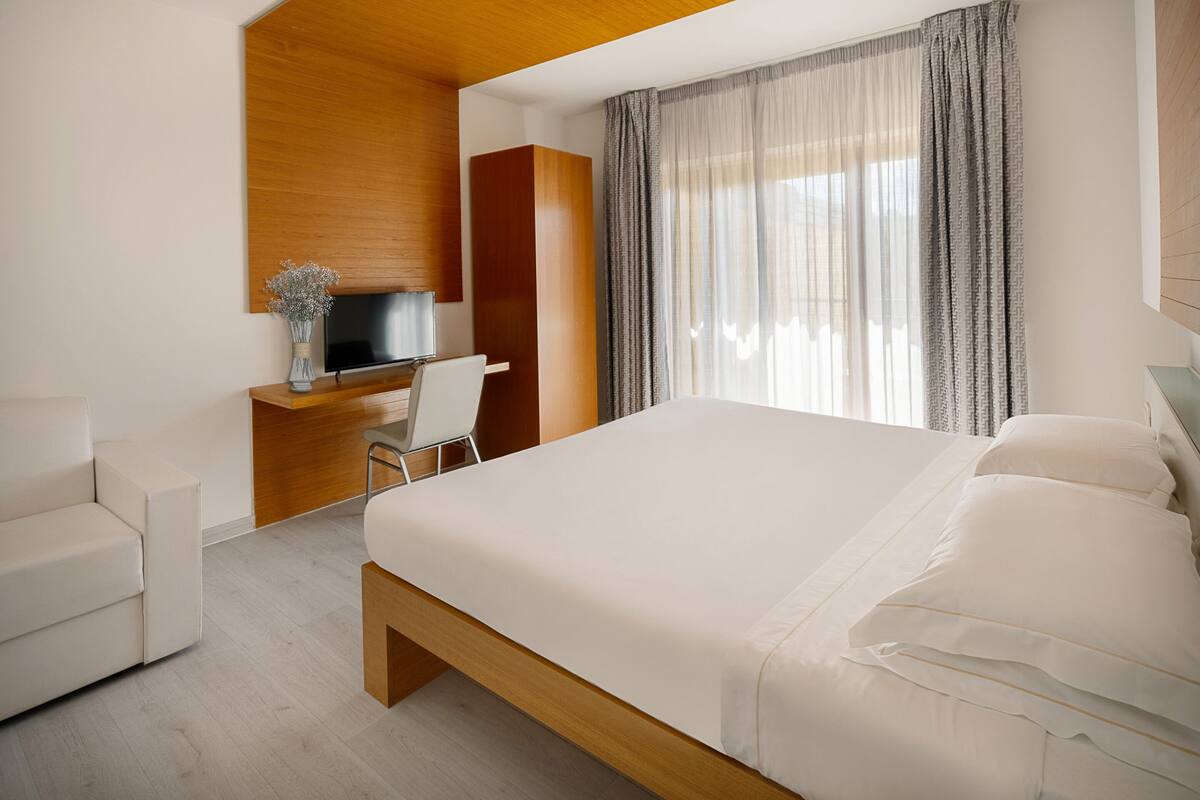 Quarto de hotel moderno com uma cama grande, uma escrivaninha com cadeira e uma televisão.