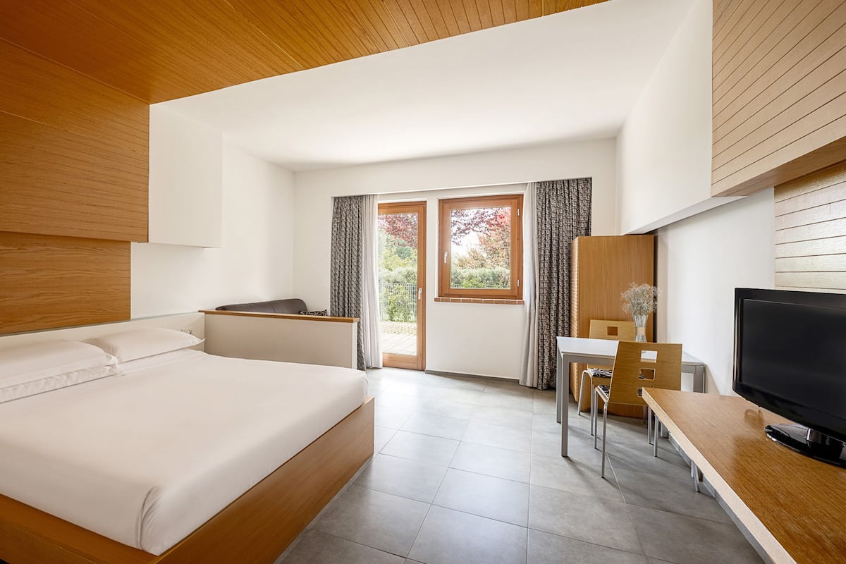 Quarto de hotel moderno com uma cama grande, uma escrivaninha, uma cadeira e uma televisão.
