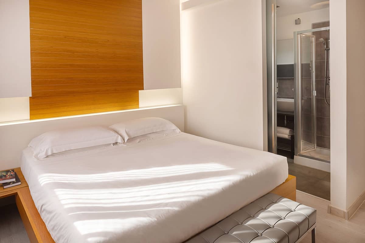 Quarto moderno com uma cama grande, cabeceira de madeira, mesa de cabeceira com um livro e closet espaçoso com porta de vidro.