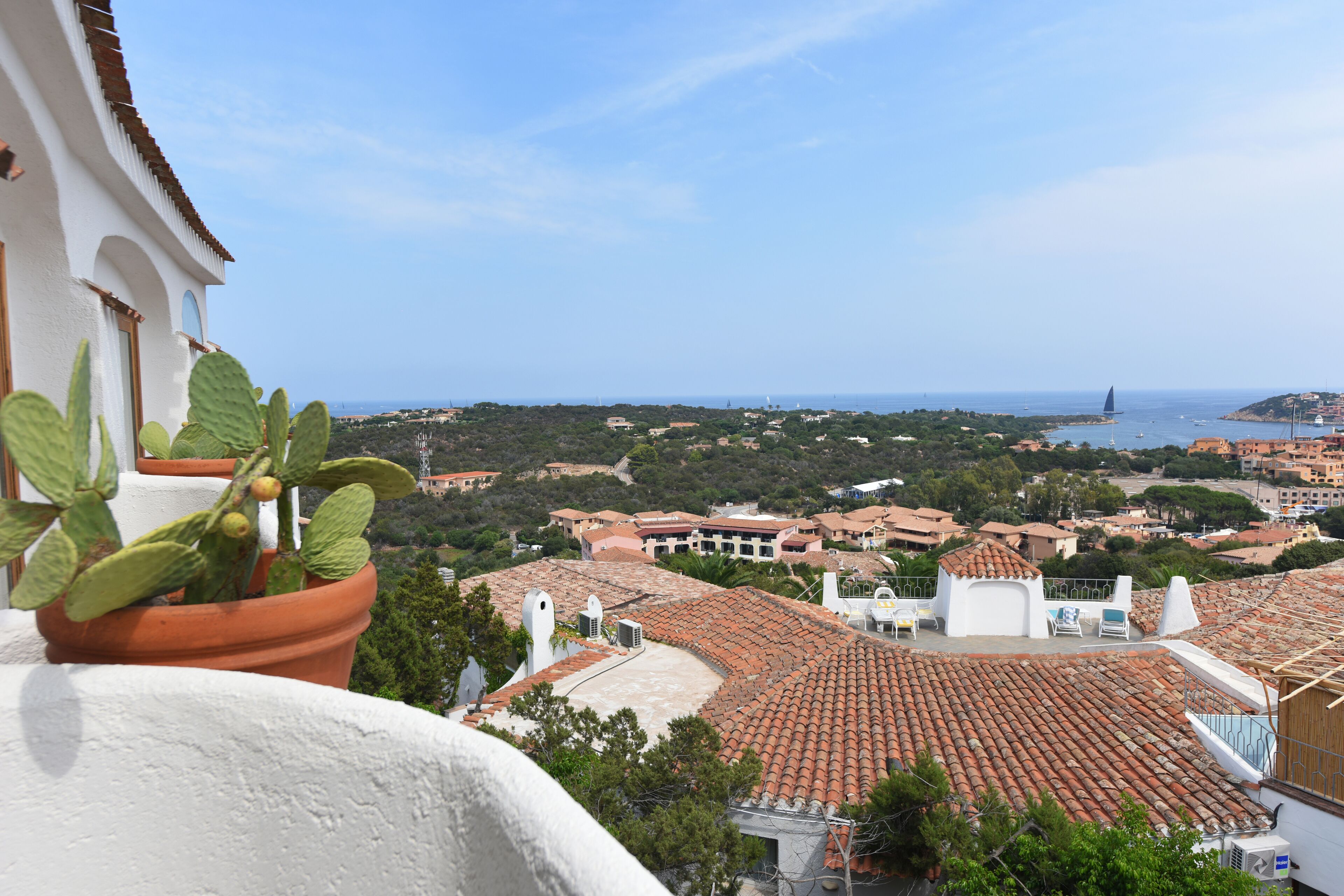 Um terraço com telhados vermelhos, um edifício branco e vista para uma vila costeira.