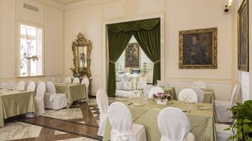 Uma sala de jantar formal, com mesas postas para uma refeição, um espelho grande e um quadro na parede.