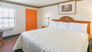 Quarto de hotel com uma cama grande, mesa de cabeceira com abajur, porta laranja, janela e quadro na parede.