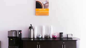 Cantinho de café com dispensador de água, cafeteira e xícara.