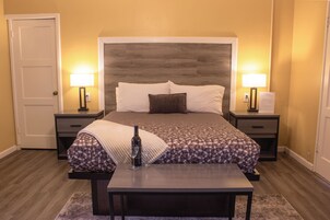 Quarto de hotel com uma cama grande, mesas de cabeceira, escrivaninha e uma cadeira.