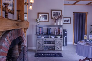 Um quarto aconchegante com lareira de tijolos, um espaço de bar com vários copos e uma máquina de café, e uma parede decorada com quadros e um relógio.