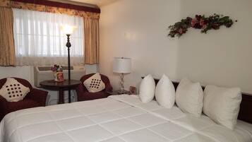 Quarto de hotel com cama, duas poltronas, uma mesa com abajur e um objeto decorativo na parede.
