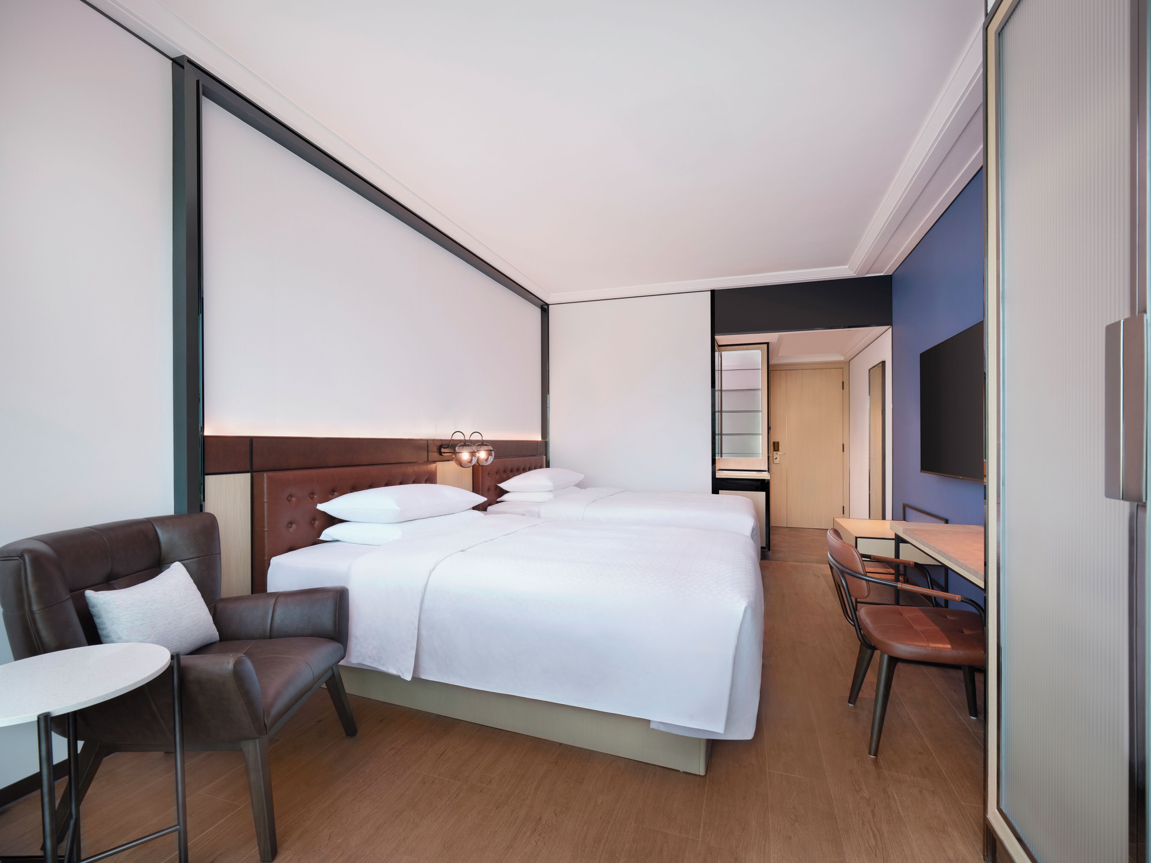 Quarto de hotel moderno com cama, escrivaninha, cadeira e televisão.