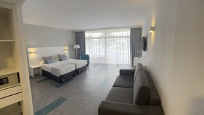 Quarto de hotel com duas camas, um sofá, uma televisão e uma escrivaninha.