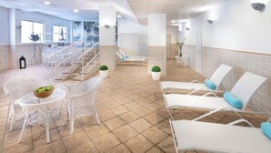 Um espaço amplo e interno com cadeiras de vime branco, uma mesa pequena com uma tigela de frutas e uma escada que leva a um andar superior.