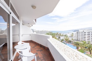 Varanda com mesa e cadeiras brancas, vista para uma piscina e edifícios.