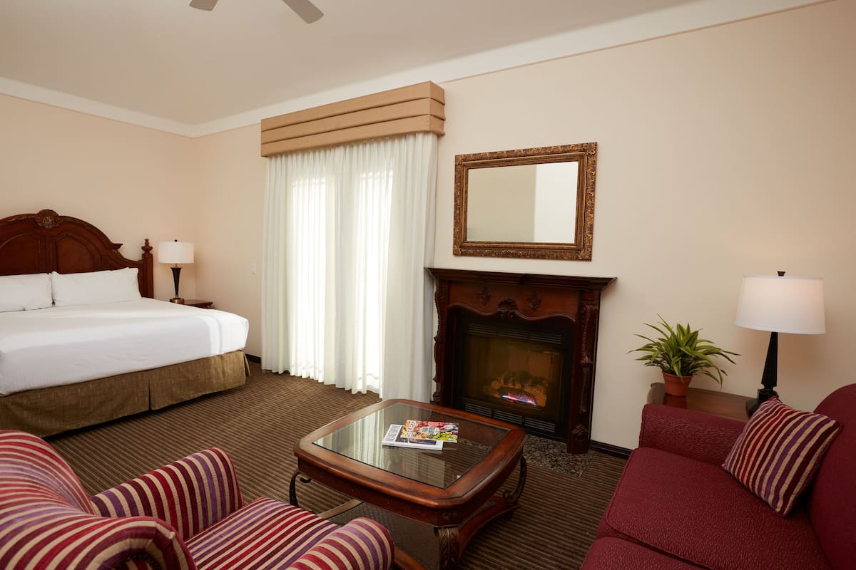 Quarto de hotel com cama, lareira, mesa de centro de vidro e dois sofás.