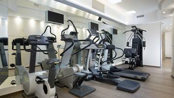 Uma academia moderna com diversos equipamentos de cardio, um espelho e uma TV de tela plana.