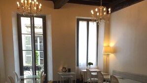 Uma sala de jantar com mesas e cadeiras de madeira, lustres e grandes janelas.