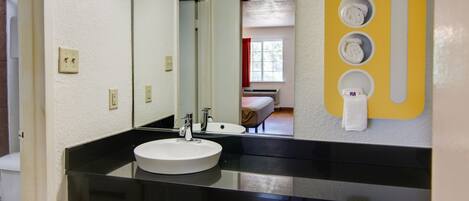 Casa de banho com uma pia branca, bancada preta e um espelho. Há três dispensadores de toalhas na parede.