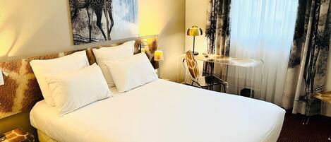 Quarto de hotel com uma cama grande, uma escrivaninha com cadeira, uma luminária e um quadro na parede.