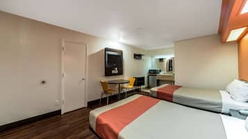 Quarto de hotel com duas camas, uma escrivaninha, uma cadeira, uma televisão e uma pequena cozinha equipada.