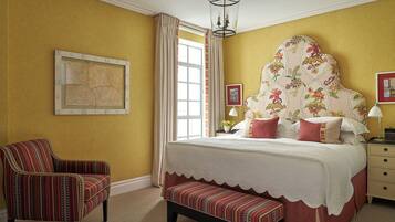 Quarto com cama, cadeira, banqueta, mesa de cabeceira e um quadro na parede.