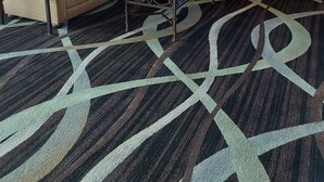 Sala de estar com sofá, mesa de centro e luminária. Há janelas com persianas e um quadro na parede.