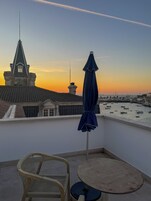 Um terraço com vista para o pôr do sol, uma cadeira, uma mesa pequena e um guarda-sol.