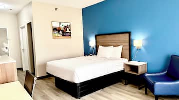 Quarto de hotel com cama, mesas de cabeceira, uma cadeira, escrivaninha e um quadro na parede.