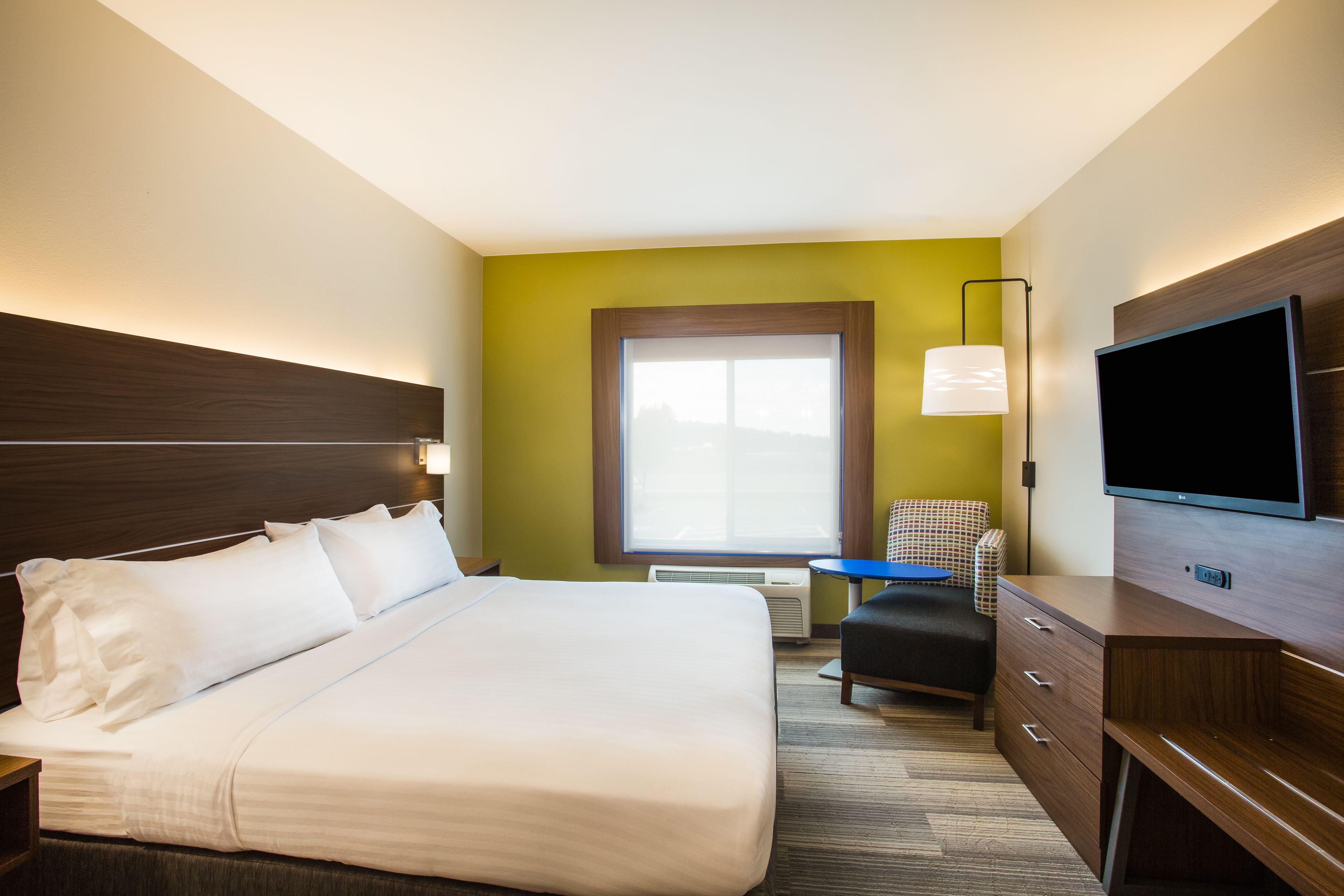 Quarto de hotel com uma cama grande, televisão de tela plana, escrivaninha e uma cadeira.