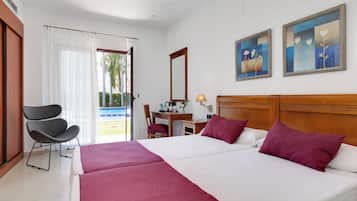 Quarto de hotel com uma cama grande, uma escrivaninha com cadeira, um espelho e duas pinturas na parede.