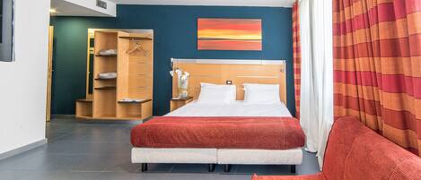 Quarto de hotel com uma cama grande, um guarda-roupa de madeira, um pequeno espaço de estar e um quadro na parede.