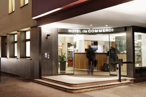 A entrada do HOTEL du COMMERCE, com uma receção e uma porta de vidro.