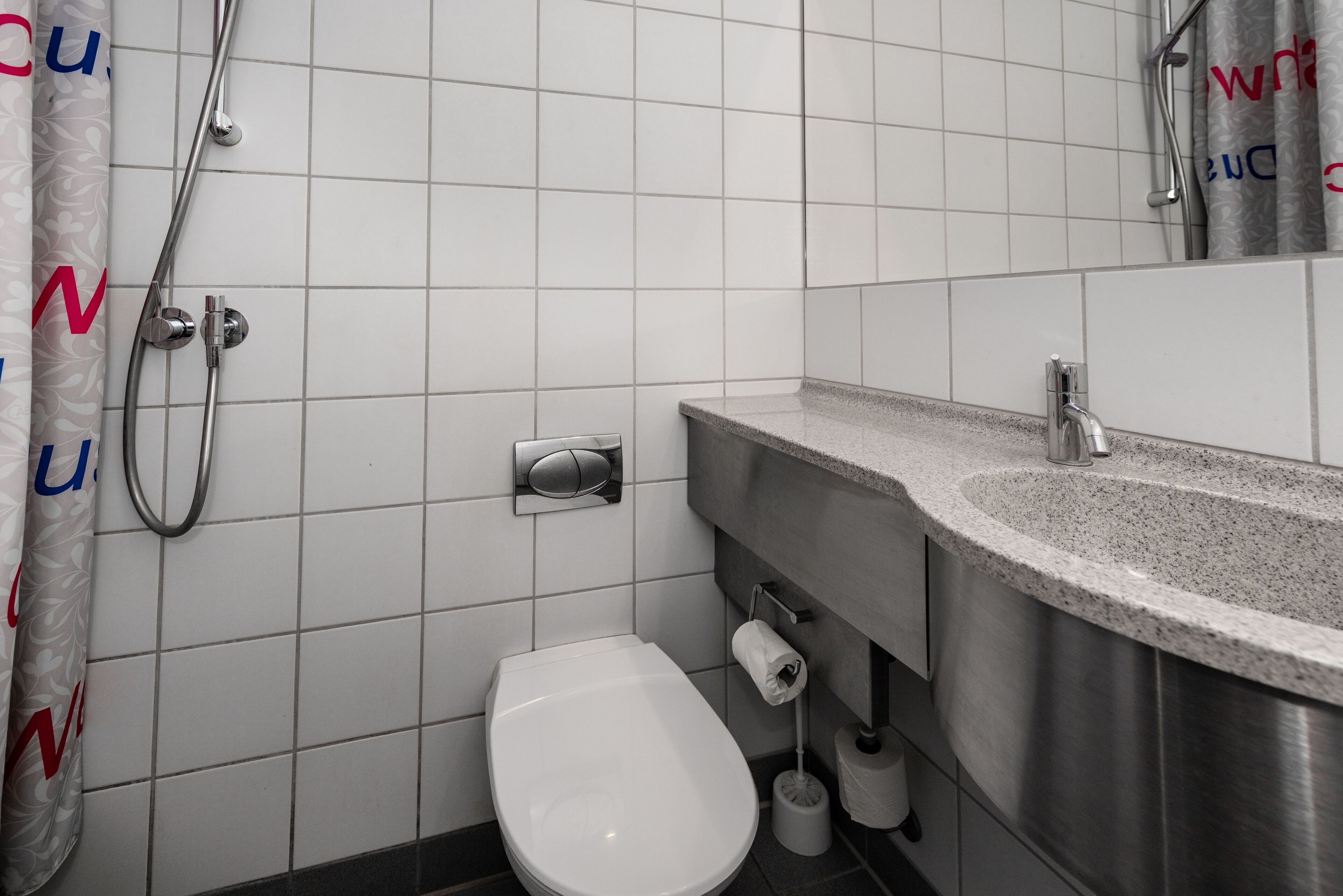 Uma casa de banho pequena e moderna com sanita branca, chuveiro e lavatório com espelho em cima.