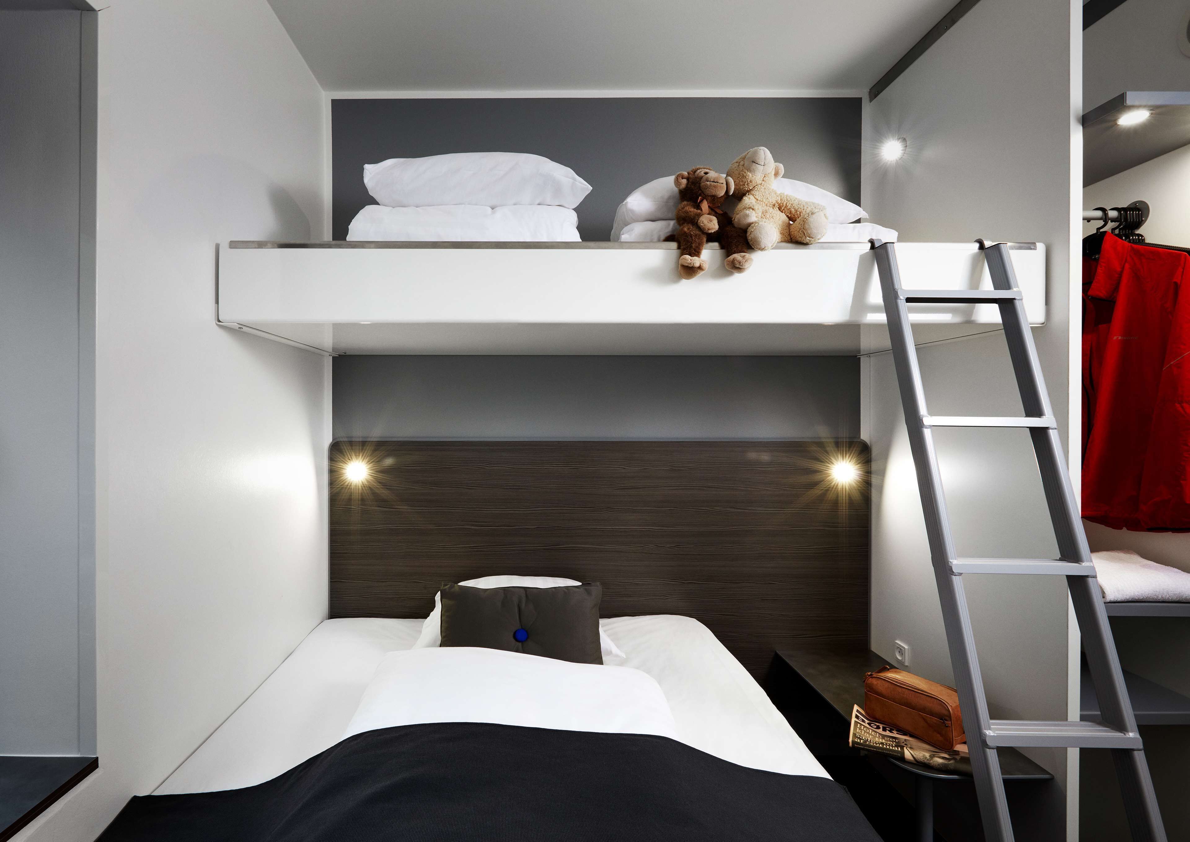 Uma cama beliche com escada, um travesseiro e bichos de pelúcia no colchão superior.