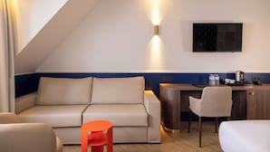 Quarto de hotel moderno com sofá, mesa redonda pequena, escrivaninha com cadeira, televisão de tela plana e máquina de café.