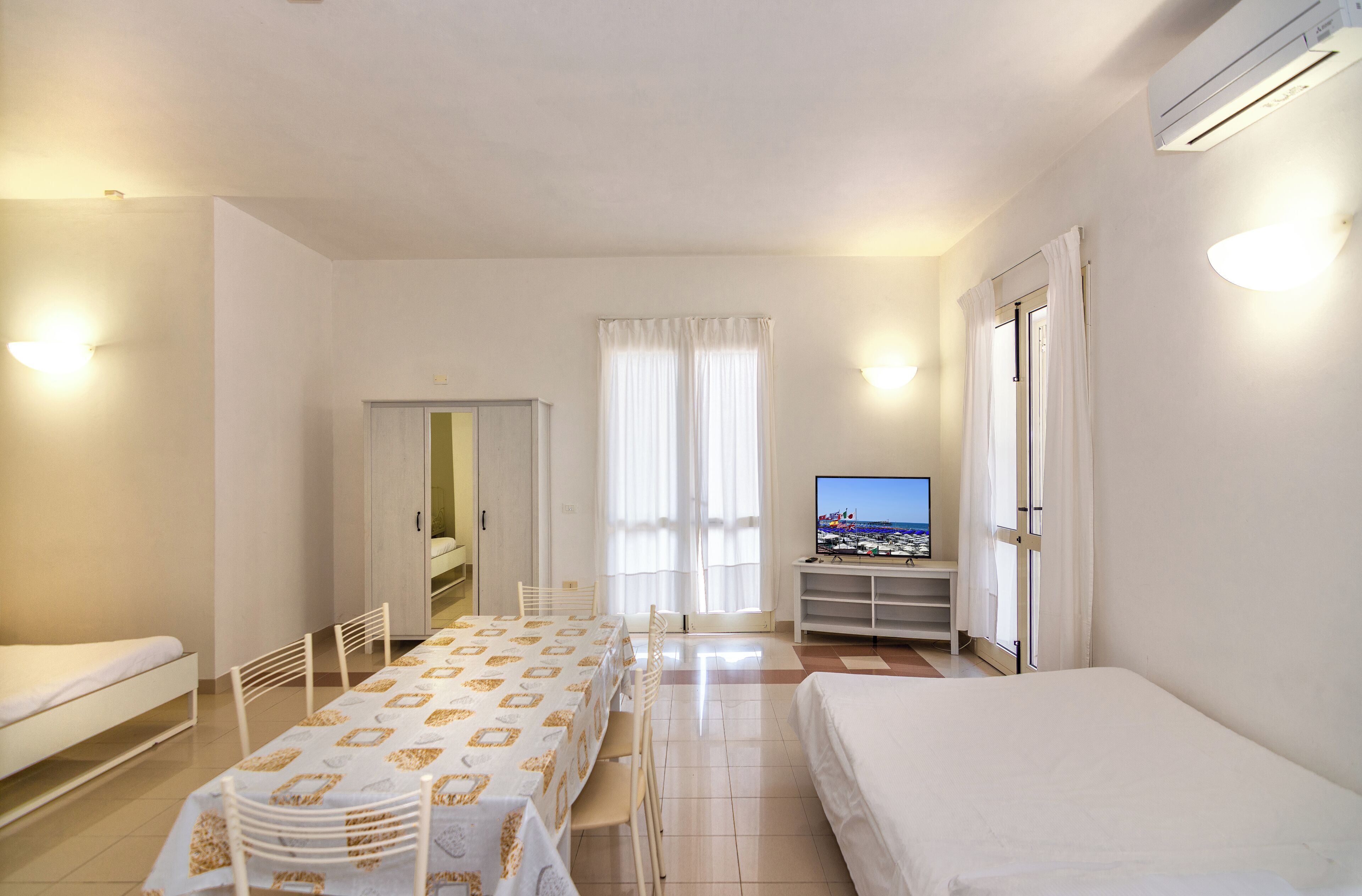 Quarto de hotel com cama, escrivaninha com televisão, mesa de jantar e vista para o mar pela janela.