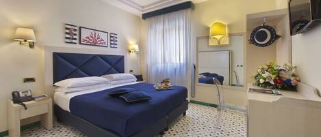 Quarto de hotel com uma cama grande, mesas de cabeceira, escrivaninha, espelho e piso estampado.