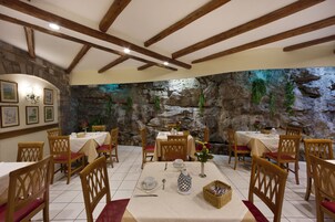 Restaurante com vigas de madeira, paredes de pedra e mesas postas para refeição.